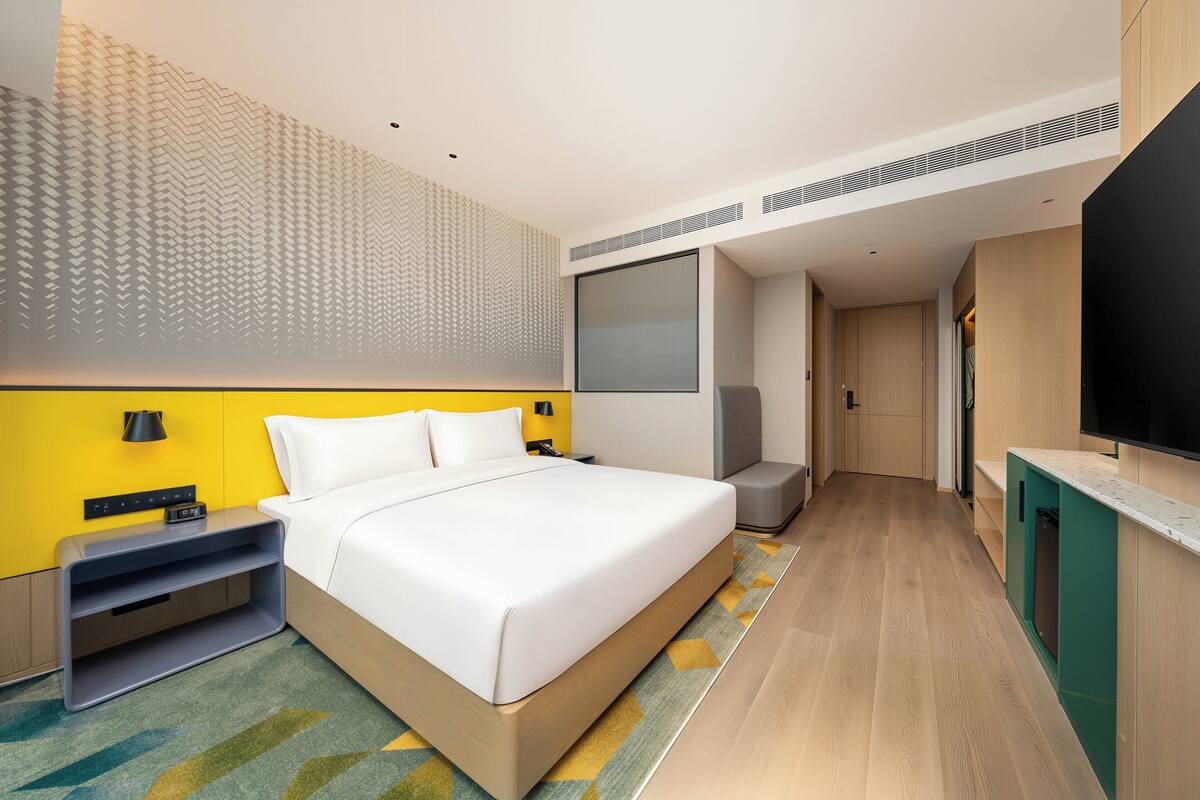 Quarto de hotel com cama, televisão, escrivaninha e banheiro.
