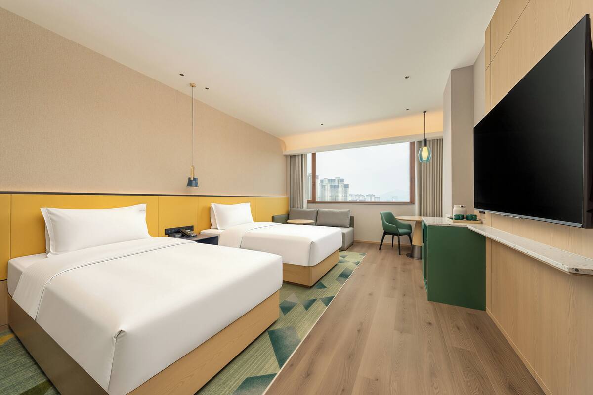 Quarto de hotel com duas camas, uma escrivaninha, televisão de tela plana e vista para a cidade.
