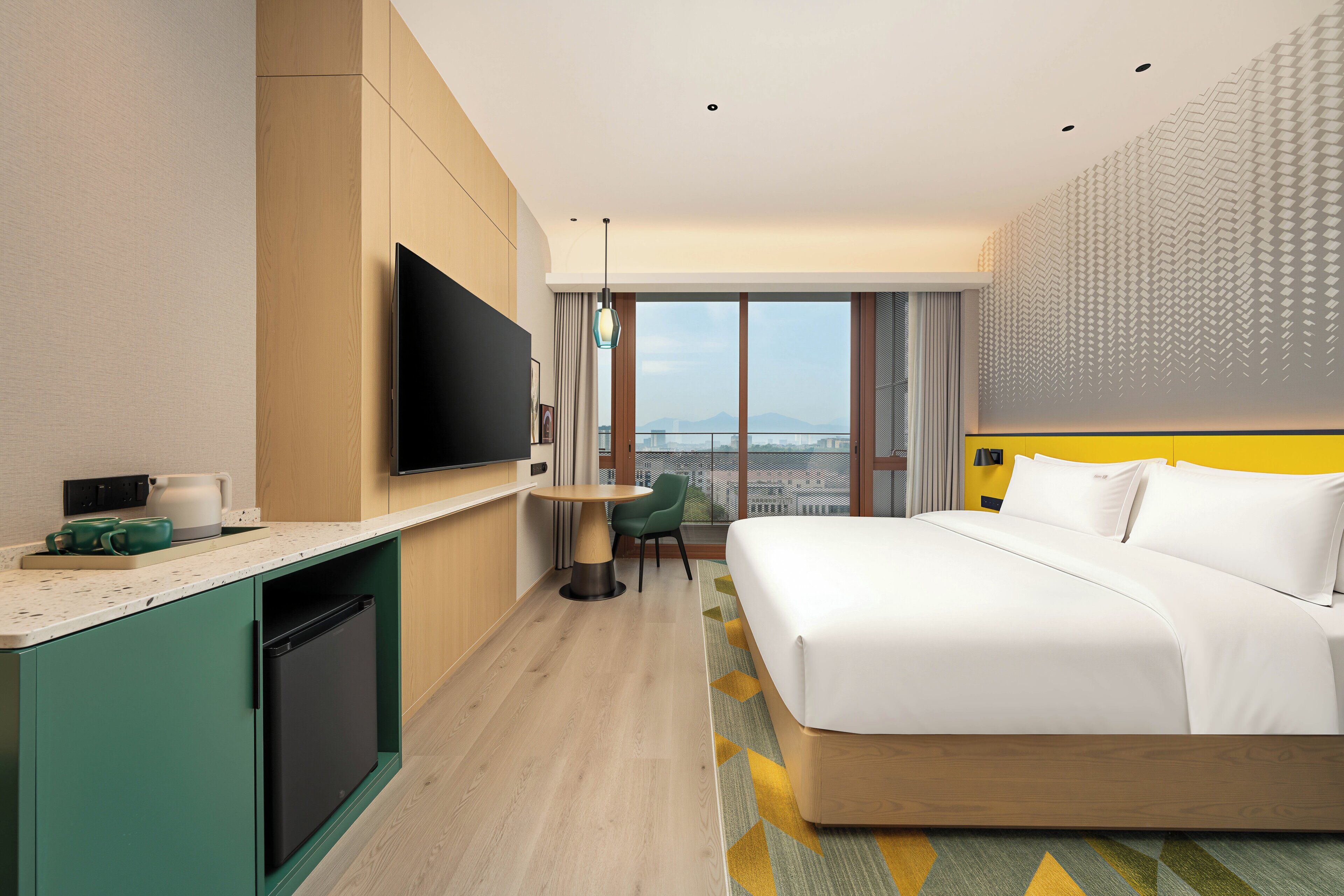 Quarto de hotel com cama, televisão, pequena cozinha, mesa de jantar e vista para a cidade.