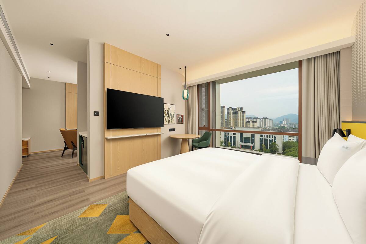 Quarto de hotel com uma cama grande, televisão presa à parede, escrivaninha e uma cadeira.