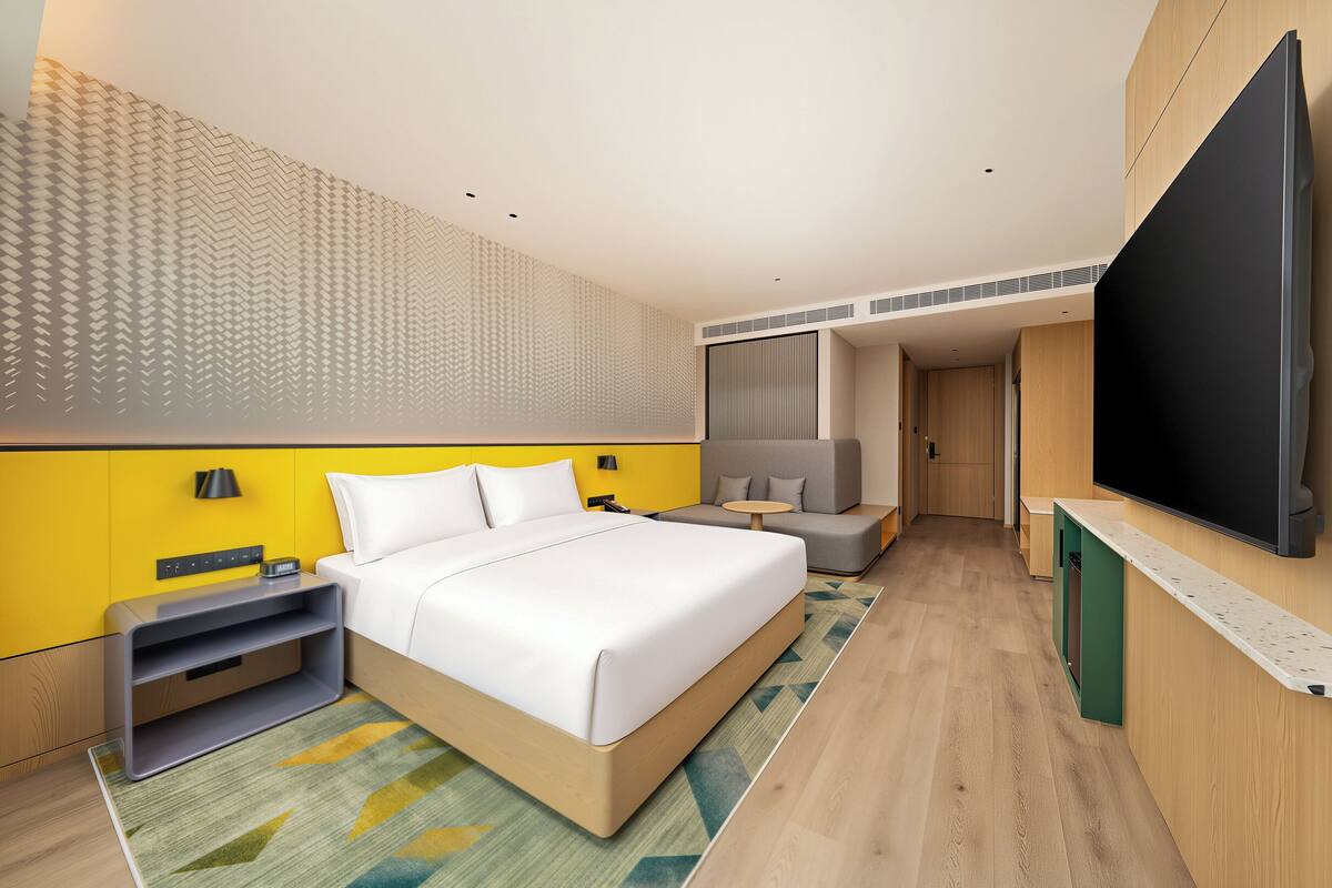 Quarto de hotel moderno com cama, área de estar, televisão e uma mesinha.