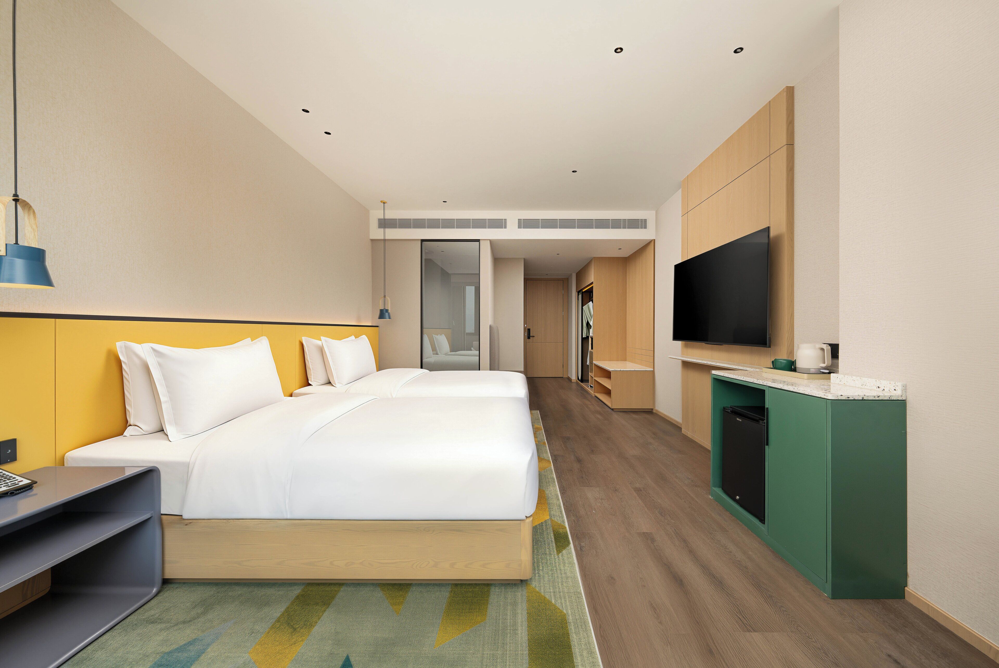 Quarto de hotel com cama, televisão, escrivaninha e uma pequena cozinha.