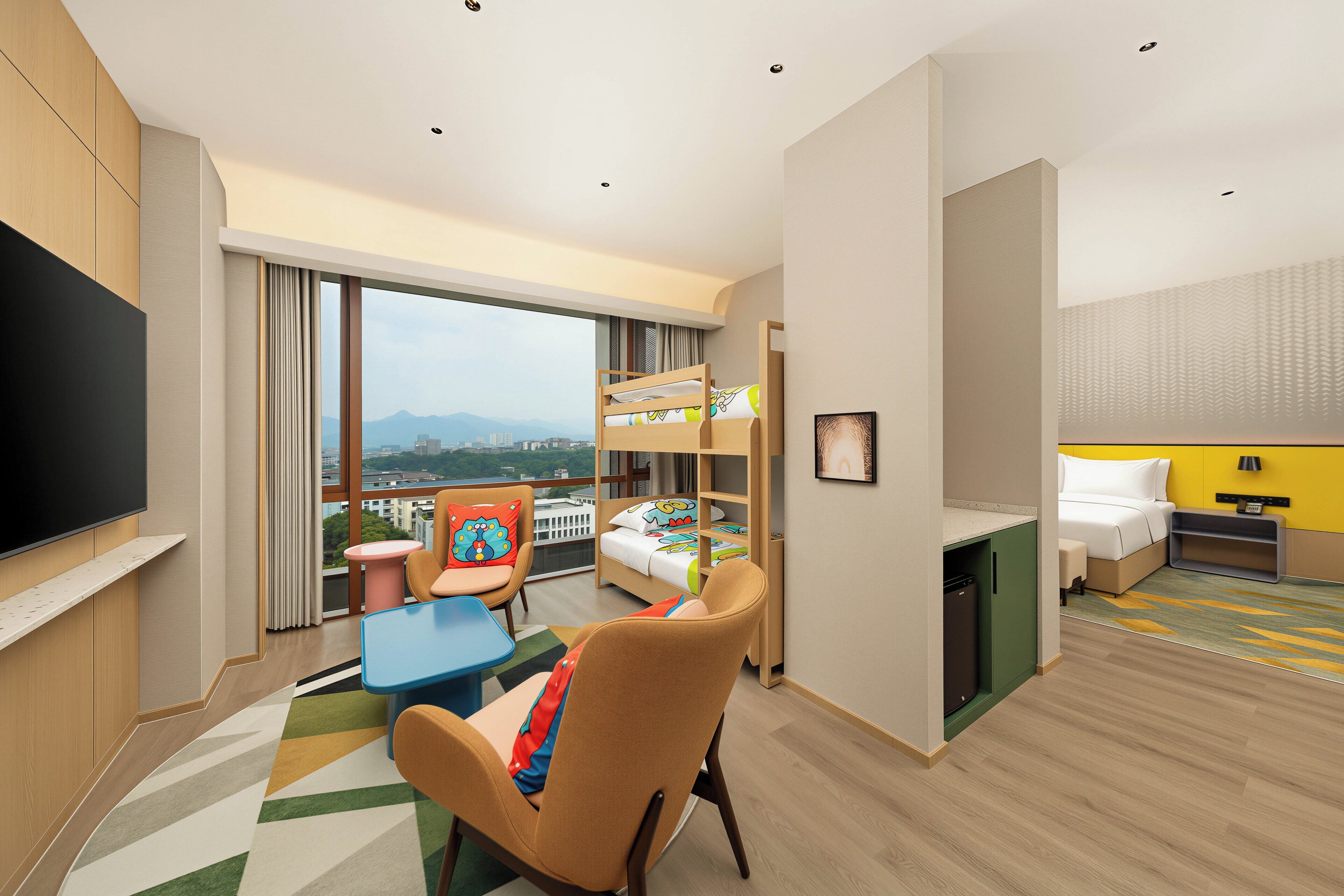 Quarto de hotel com televisão, beliches, escrivaninha e vista da cidade.