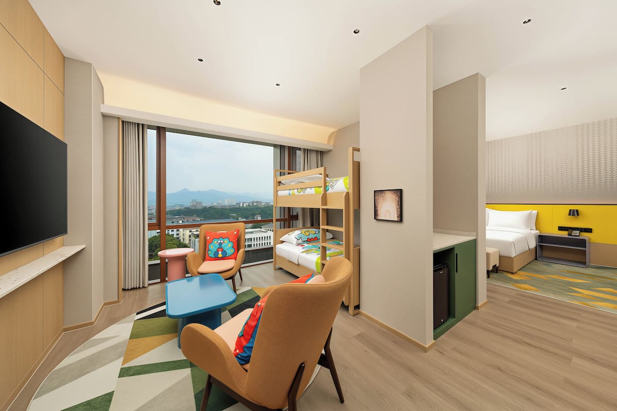 Quarto de hotel com televisão, beliches, escrivaninha e vista da cidade.