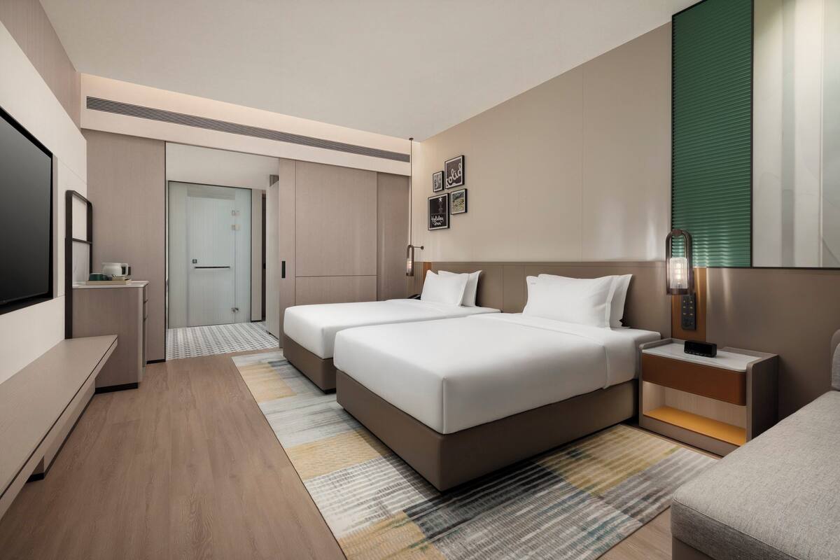 Quarto de hotel moderno com uma cama grande, mesas de cabeceira, televisão e uma porta para o banheiro.