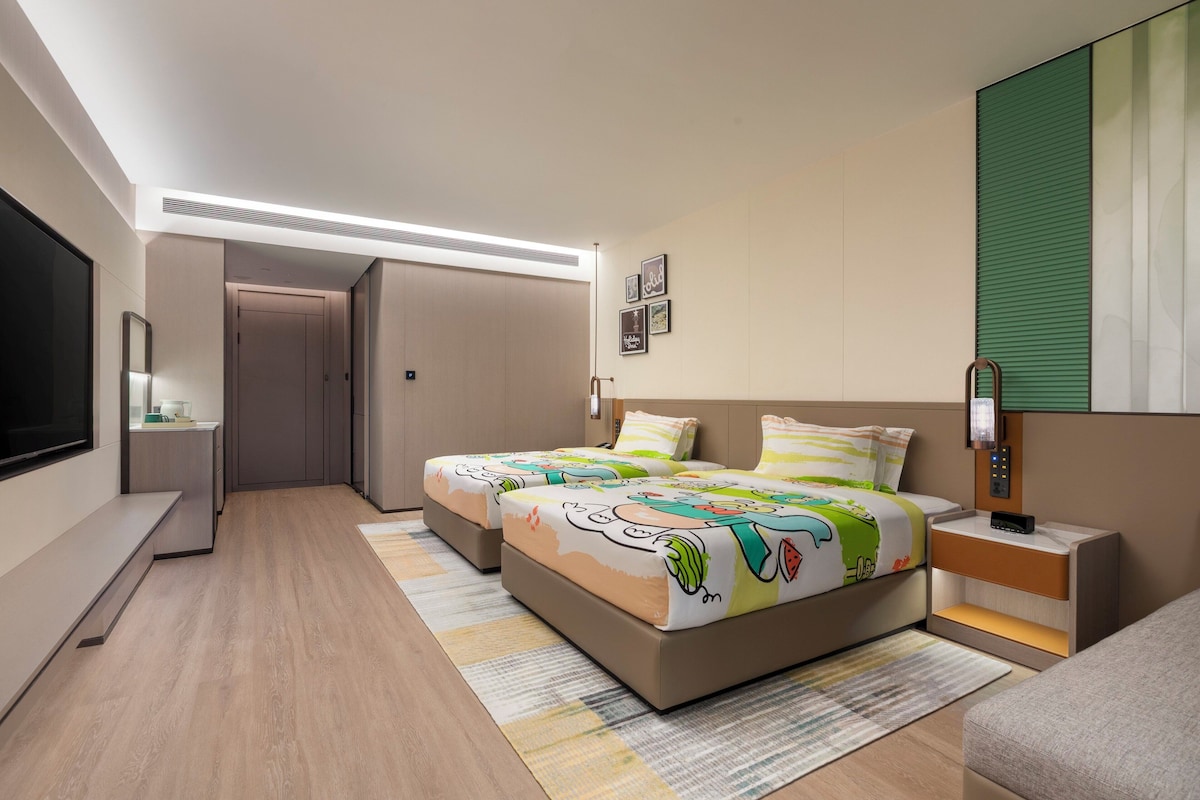 Quarto de hotel moderno com duas camas, televisão de tela plana, mesa de cabeceira e um espelho grande.