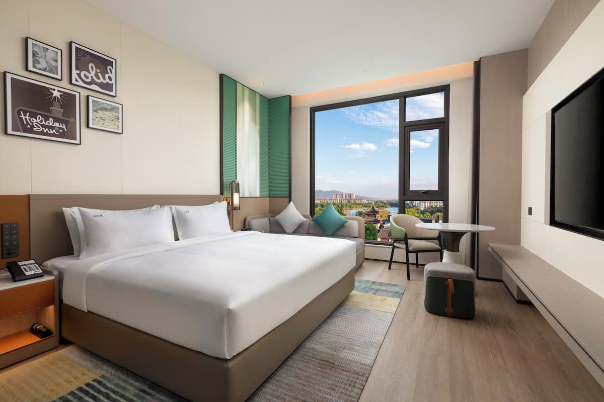 Quarto de hotel com uma cama grande, uma escrivaninha, uma cadeira, uma televisão e vista para a cidade.