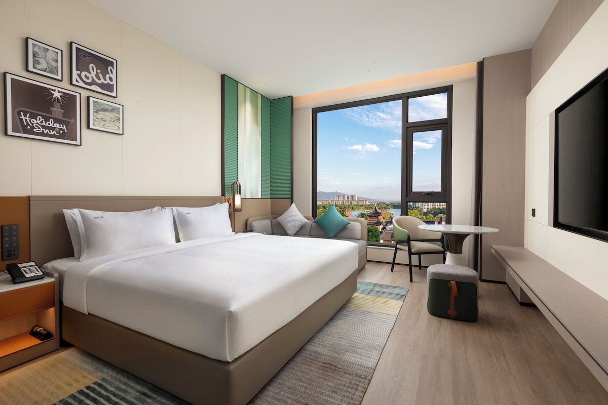Quarto de hotel com uma cama grande, uma escrivaninha, uma cadeira, uma televisão e vista para a cidade.