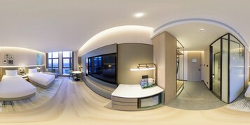 Quarto de hotel moderno com layout curvo, uma televisão grande, área de estar e vista para a cidade.