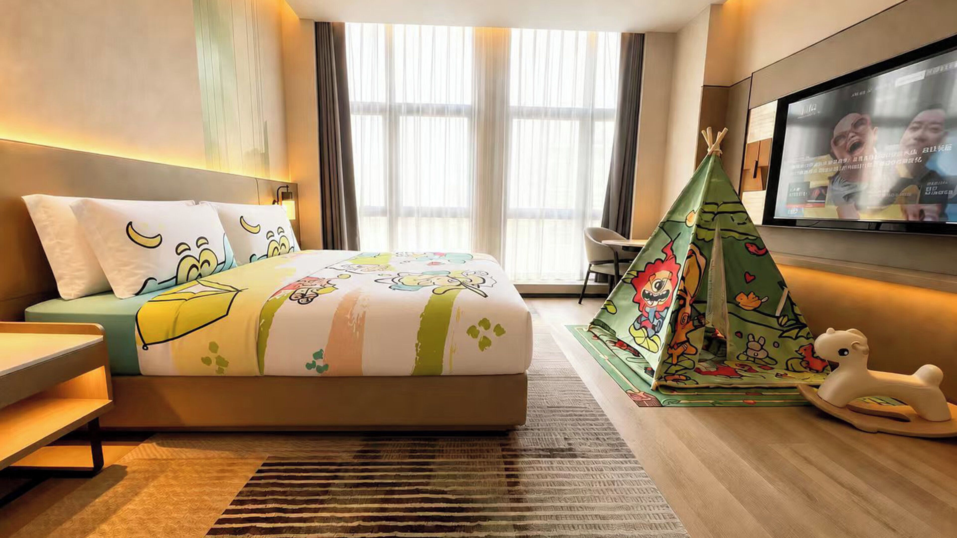 Quarto de hotel com cama, televisão, uma tenda verde e uma mesa de madeira.