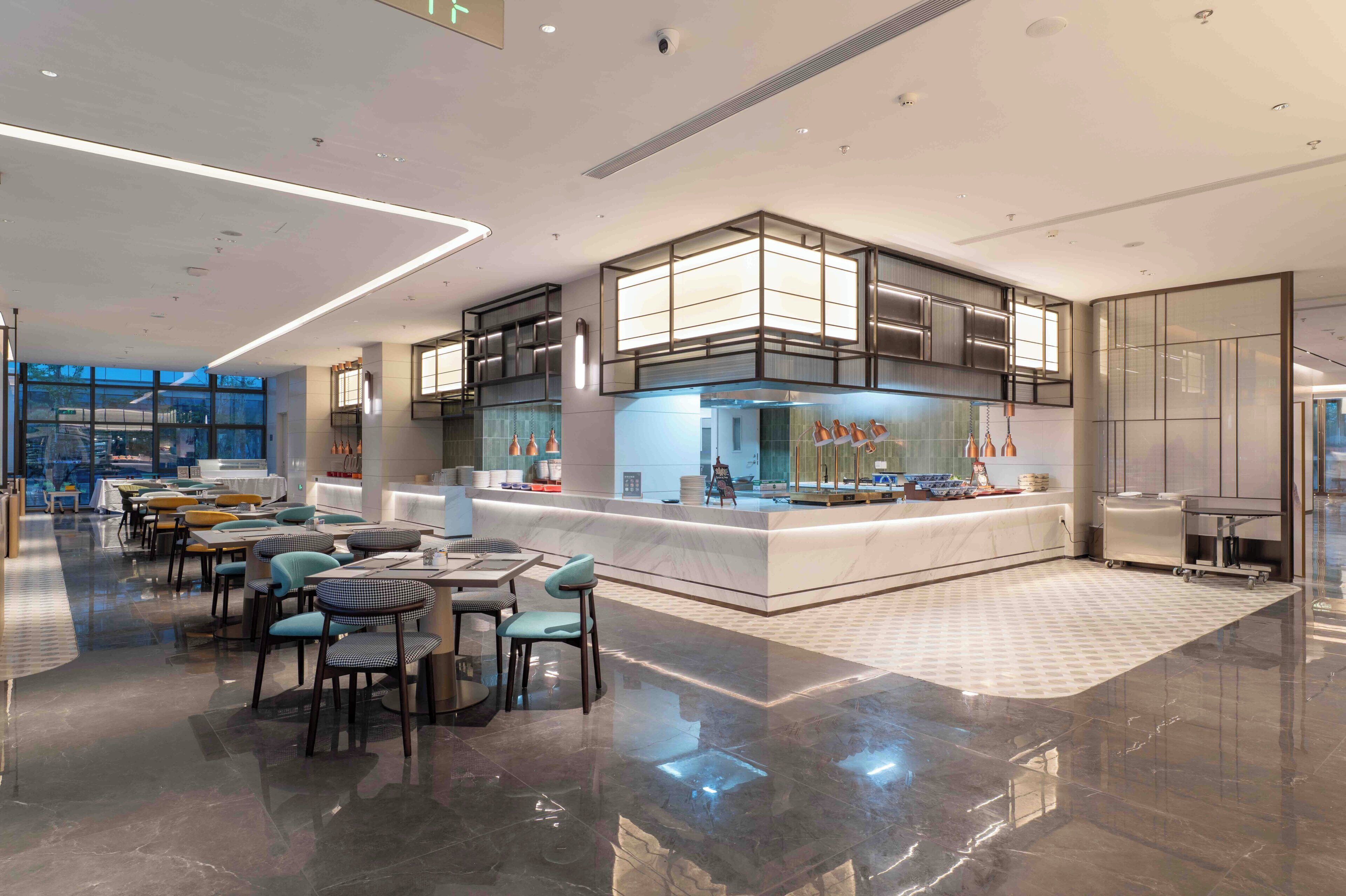 Um lobby de hotel moderno com bar central, espaços de estar e vista através de grandes janelas.