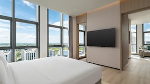 Quarto de hotel moderno com uma cama grande, televisão de tela plana na parede e vista para a cidade através de amplas janelas.