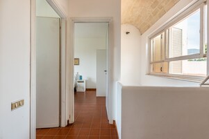 Um corredor com piso de azulejos, uma porta branca e uma janela com persianas.