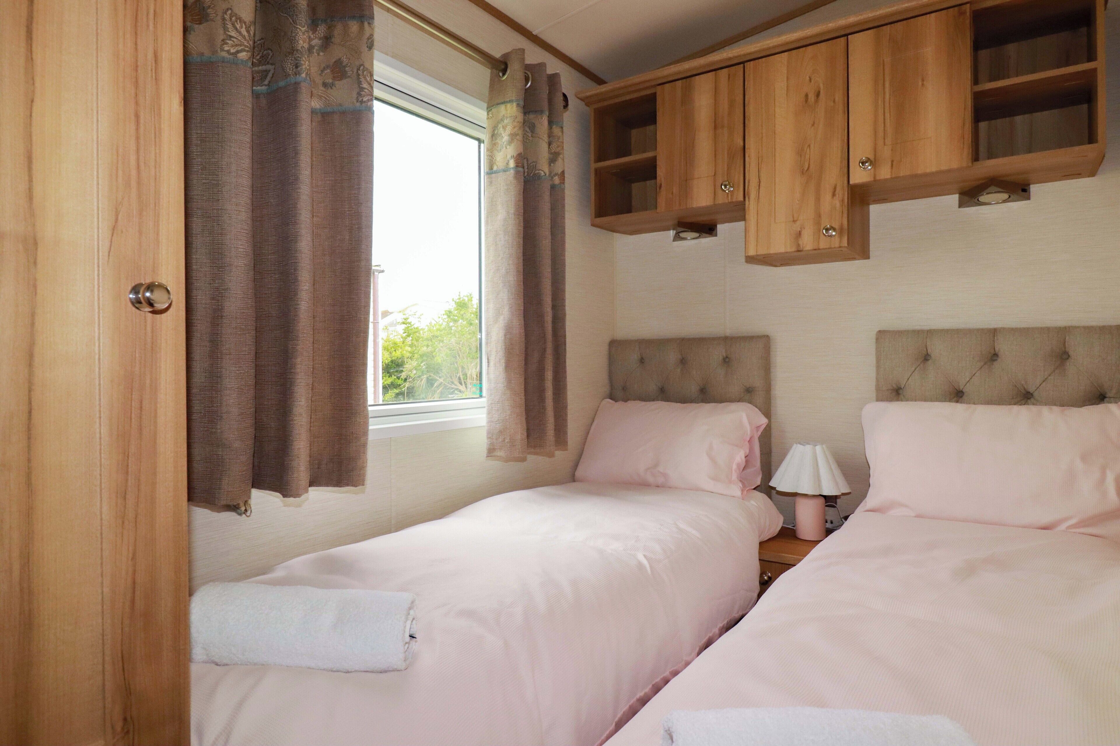 Quarto com duas camas, armários de madeira acima, uma janela com cortinas e um abajur.