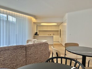 Uma sala moderna com sofá, uma mesa de jantar e área de cozinha ao fundo.