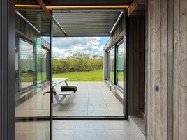 Um pátio moderno com porta de vidro, um banco branco e vista para uma área gramada.