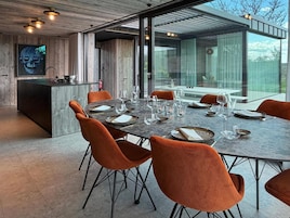 Uma sala de jantar moderna com uma mesa grande, cadeiras laranja e vista para o exterior.
