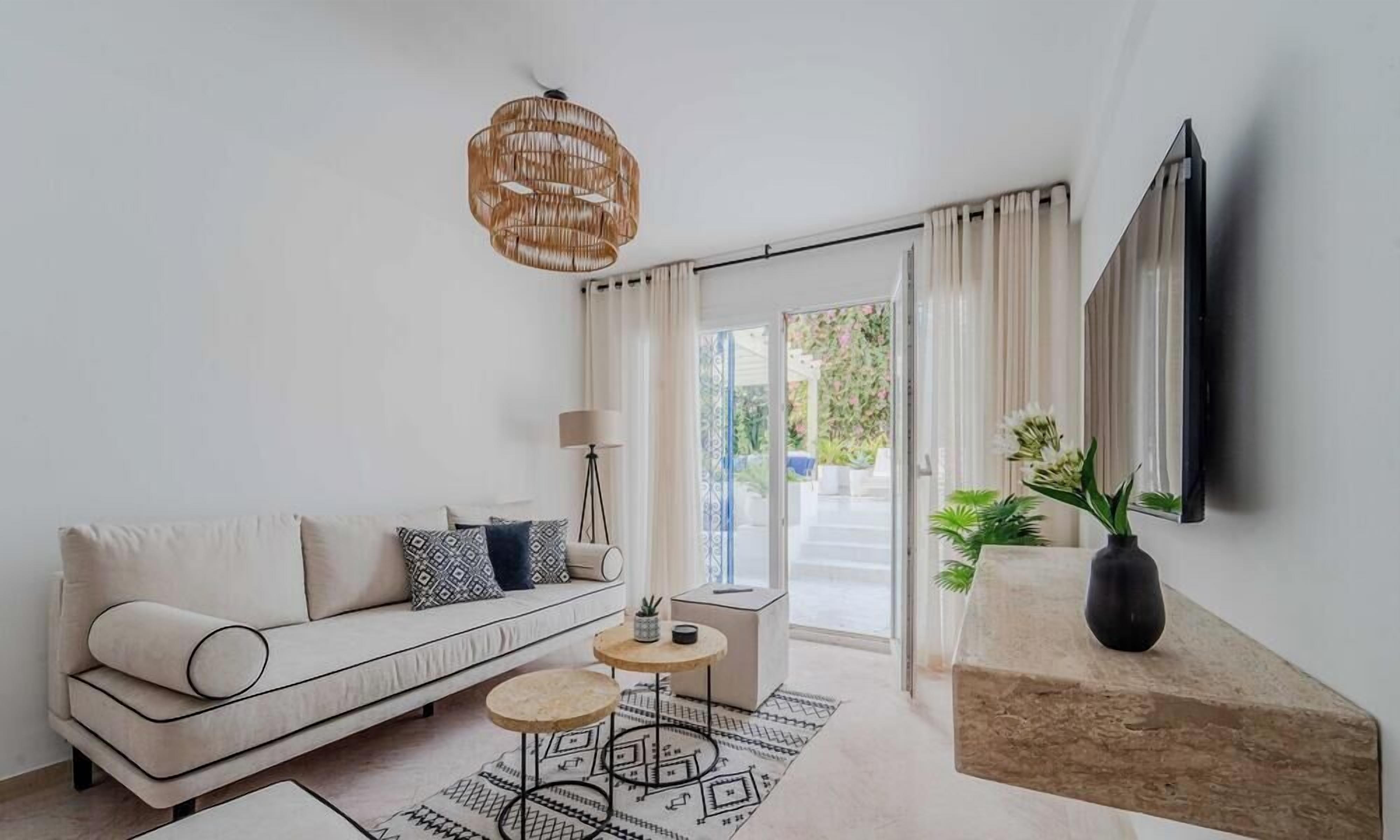 Uma sala de estar moderna com sofá, mesa de centro redonda, abajur e uma TV grande fixada na parede.
