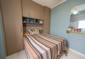 Quarto com cama, guarda-roupa, estantes e espelho.