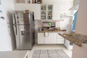 Uma cozinha moderna com geladeira de aço inoxidável, armários brancos, bancada de granito e painel de azulejos.