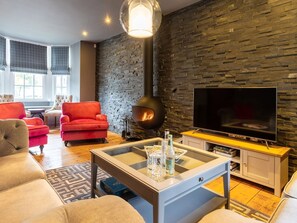 Uma sala de estar moderna com parede de pedra, lareira, TV e poltronas vermelhas.