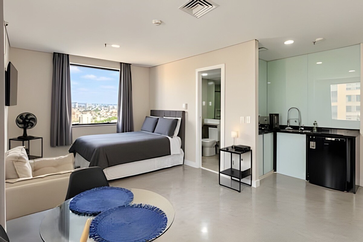 Quarto de hotel moderno com cama, escrivaninha, cadeira e vista da cidade.