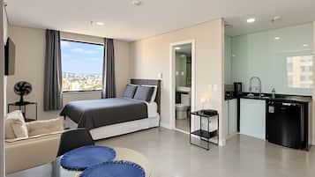 Quarto de hotel moderno com cama, escrivaninha, cadeira e vista da cidade.
