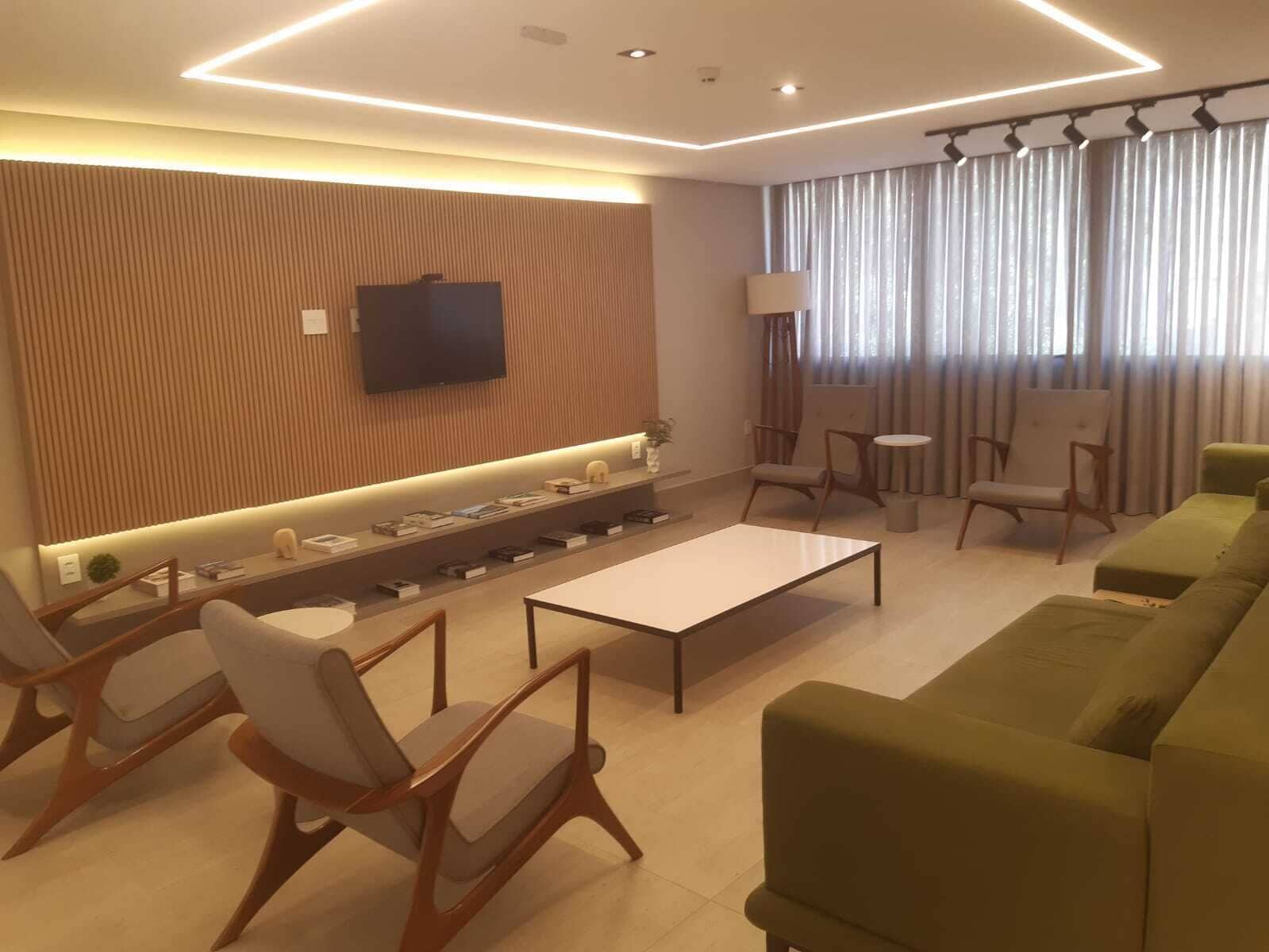 Uma sala de estar moderna com uma televisão de tela plana, um sofá, cadeiras, uma mesa de centro e uma estante de livros.