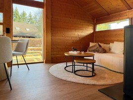 Interior acolhedor de uma cabana com uma mesa redonda, um sofá e uma poltrona.