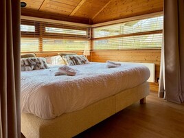 Quarto com painéis de madeira, uma cama grande, piso de madeira e uma janela com persianas.
