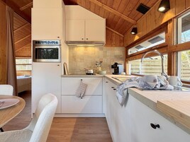 Uma cozinha compacta com armários brancos, forno embutido, cafeteira e janela com vista para um deck de madeira.