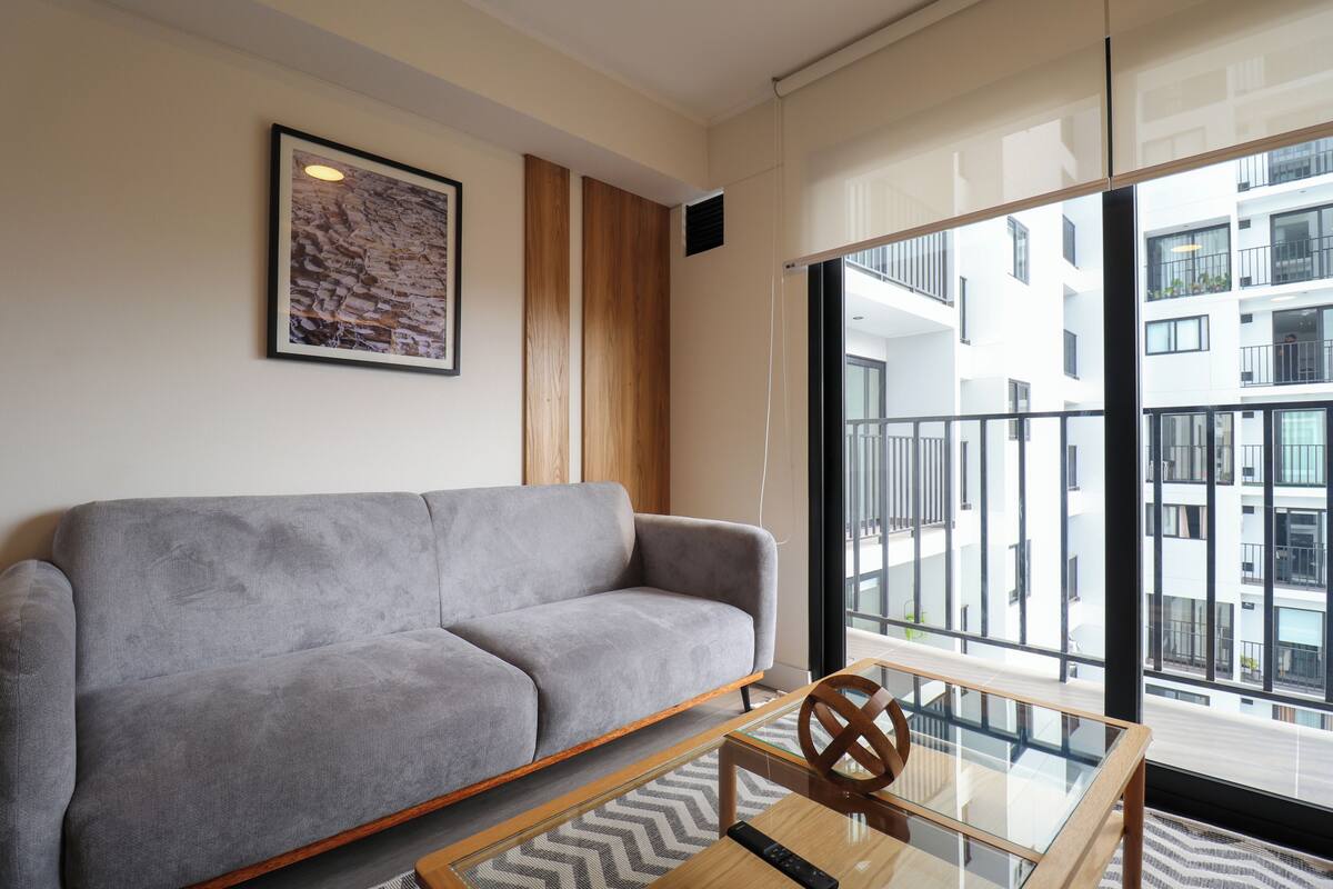 Uma sala de estar moderna com um sofá cinzento, uma mesa de centro de vidro e um quadro pendurado na parede.
