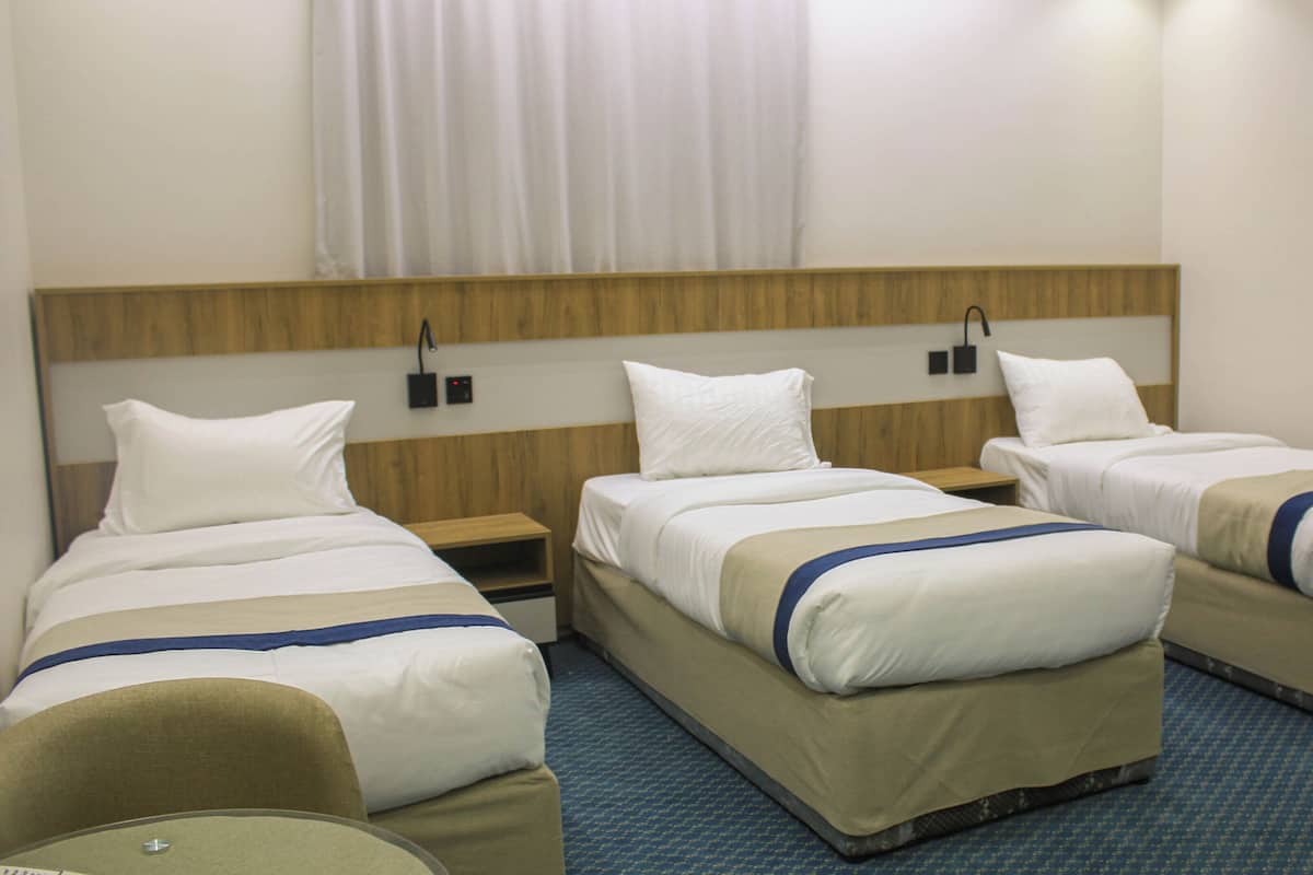 Quarto de hotel com três camas, cabeceira de madeira, mesas de cabeceira e tapete azul.