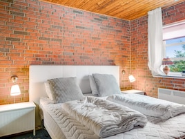 Quarto com parede de tijolos, cabeceira branca, duas luminárias de apoio, janela com cortina e cama com roupa de cama branca.