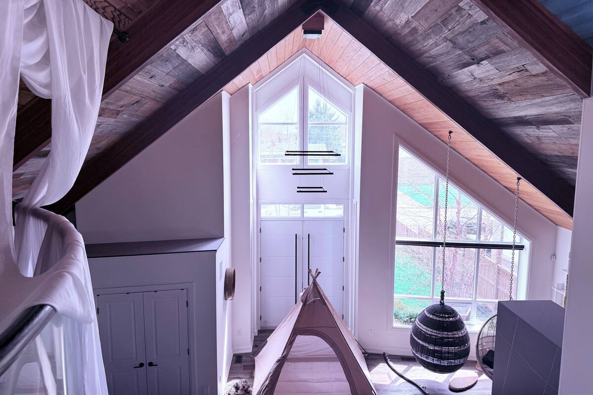 Um quarto com pé-direito alto, estrutura de vigas de madeira, espaço tipo tenda e uma cadeira esférica suspensa.
