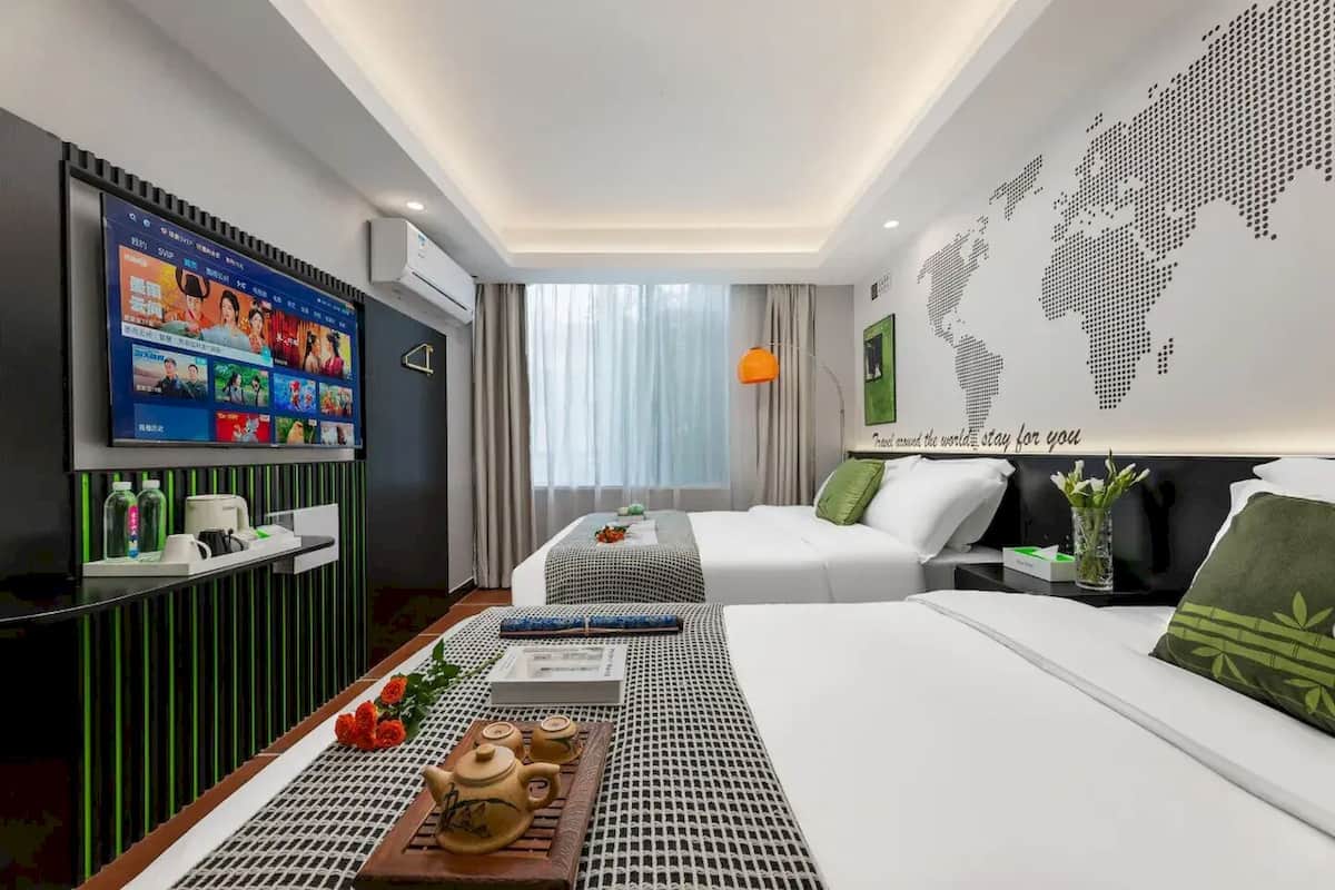 Quarto de hotel com televisão, um mapa-múndi na parede, cama, sofá e mesa com um conjunto de bules.