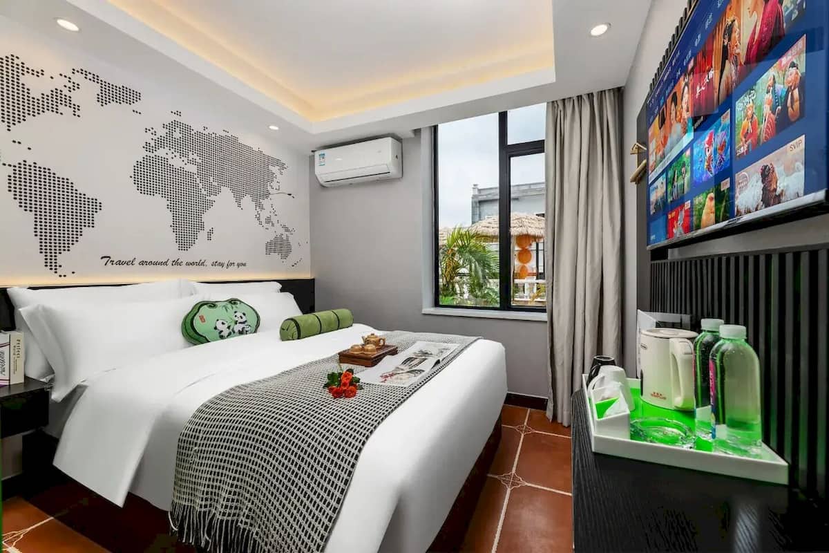 Quarto de hotel com cama, um mapa-múndo na parede, televisão e janela com vista para edifícios.