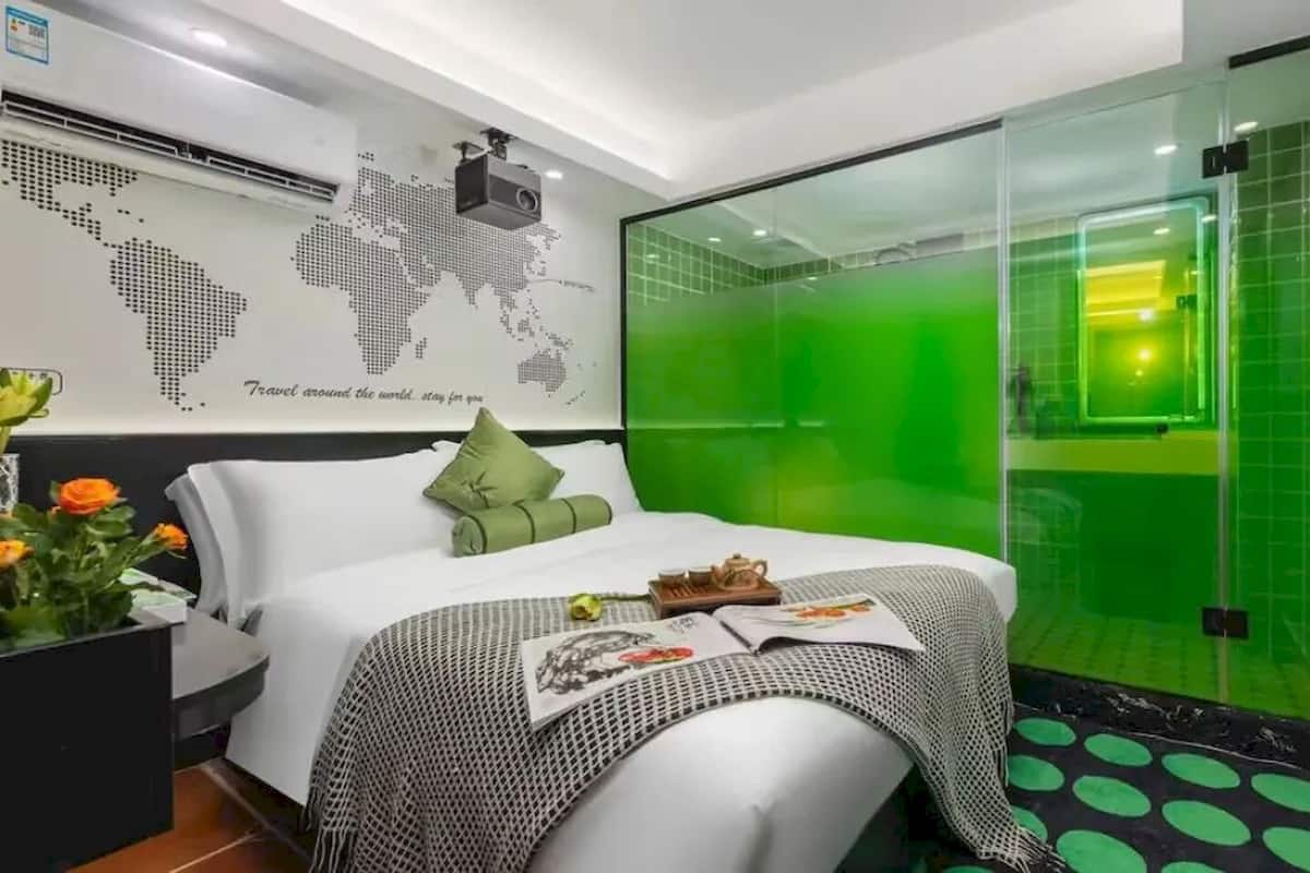 Quarto de hotel com uma cama, um mapa-múndi na parede, um painel de vidro com tonalidade esverdeada e uma cama com travesseiro verde.