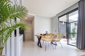Sala de estar moderna com uma mesa de jantar e cadeiras, uma grande porta de vidro deslizante que dá para uma varanda e um vaso com planta.