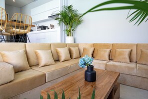 Uma sala de estar moderna com um sofá bege, mesa de centro de madeira e uma planta em vaso.