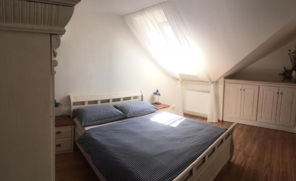 Quarto com cama, mesas de cabeceira, luminária, guarda-roupa e janela com cortinas.