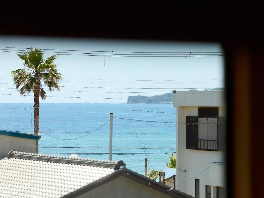 Vista costeira com palmeira, um edifício com janelas gradeadas e céu claro.