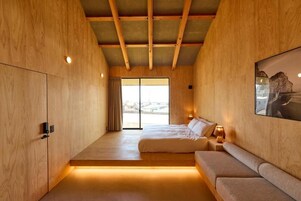 Quarto moderno com paredes de madeira, uma cama, um banco e uma janela grande.