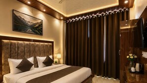 Quarto de hotel moderno com uma cama grande, ventilador de teto, televisão montada e vista para as montanhas.