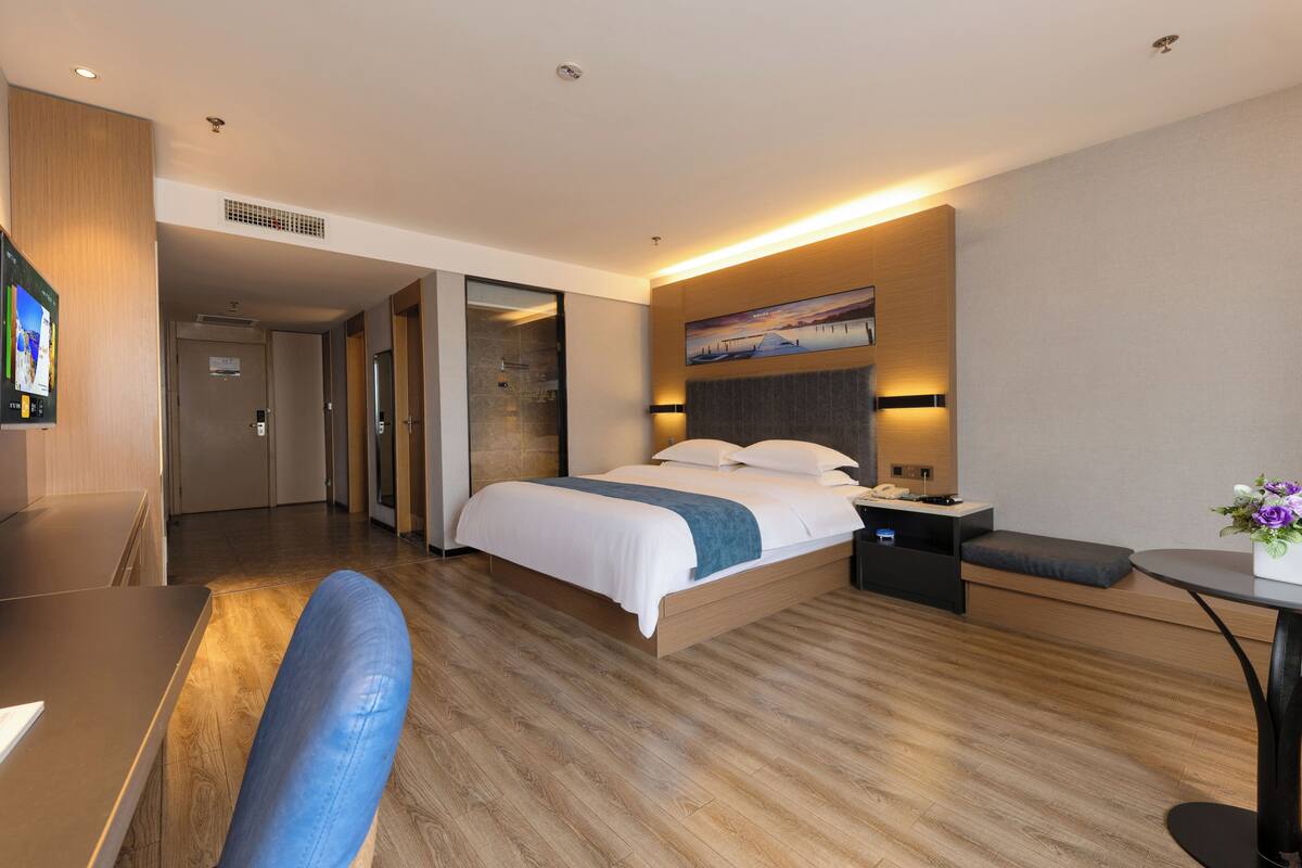 Quarto de hotel moderno com cama, mesa de cabeceira, escrivaninha e um espaço para sentar.