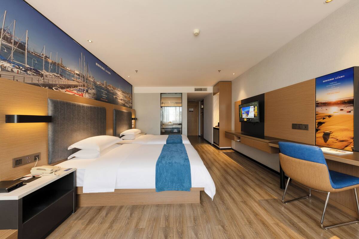 Quarto de hotel com cama, escrivaninha, cadeira, televisão e um grande mural na parede.