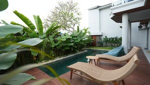 Uma área na beira da piscina com espreguiçadeiras, um deck de madeira e muita vegetação.