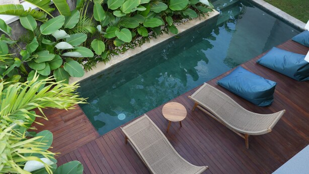 Área de piscina com espreguiçadeiras e uma pequena mesa, rodeada por vegetação exuberante.