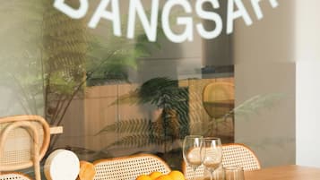 Uma área de jantar com mesa posta para quatro pessoas, com cadeiras de vime, uma cesta de frutas e um copo de suco de laranja.