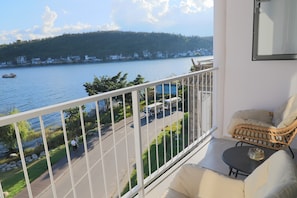 Uma varanda com vista para um lago, uma cadeira de vime e uma mesa pequena.